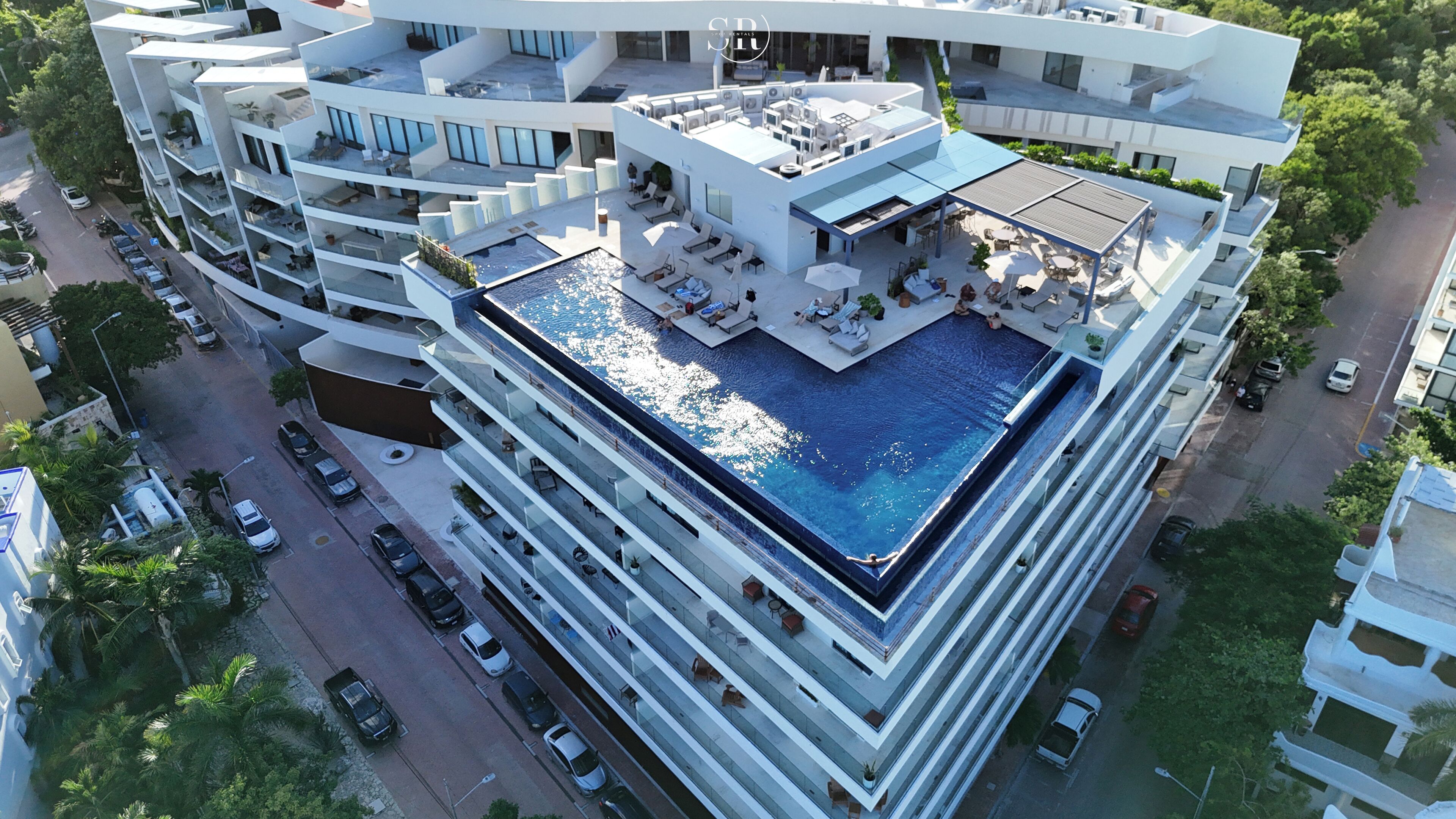 Um hotel moderno de vários andares, com piscina no terraço, várias varandas e vista para a rua.