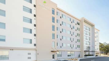Edifício de hotel com vários andares, fachada bege, várias janelas e estacionamento com vagas demarcadas.