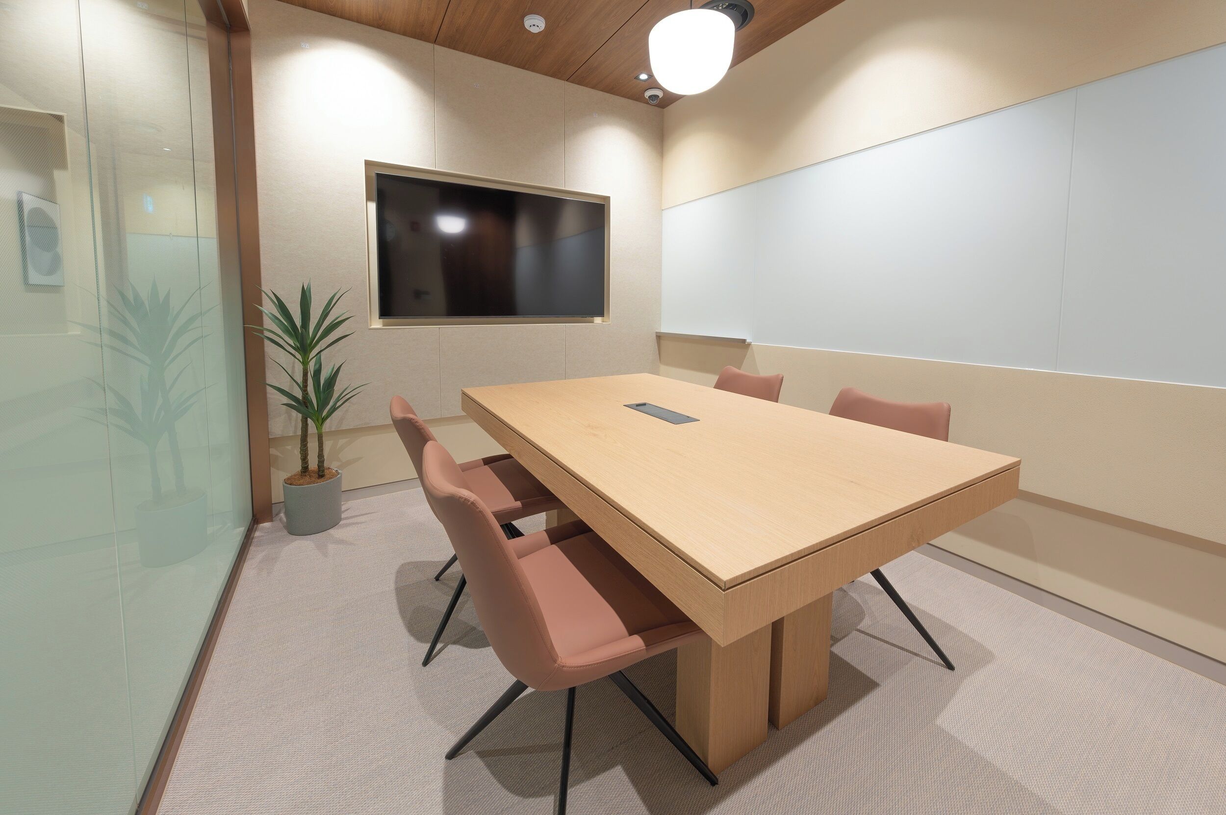Uma sala de conferências com uma mesa grande, quatro cadeiras, uma planta em vaso e um janelão.