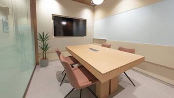Uma sala de conferências com uma mesa grande, quatro cadeiras, uma planta em vaso e um janelão.