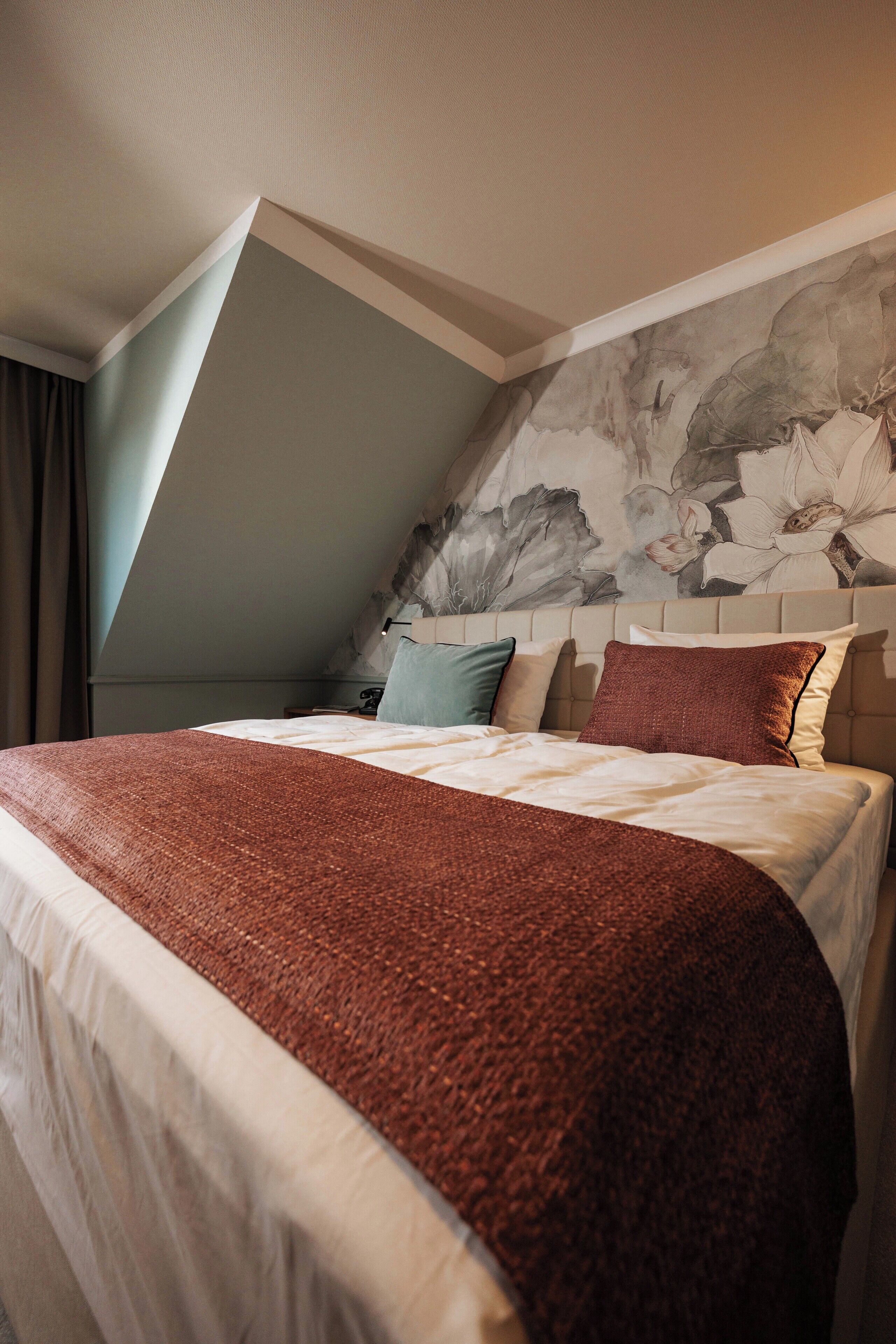 Quarto com cama, almofadas, cabeceira e parede com mural floral.