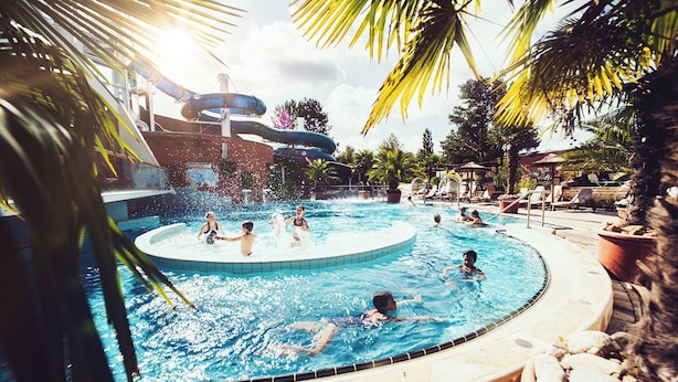 Piscina com várias pistas, palmeiras e um tobogã ao fundo.