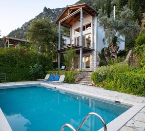 Uma villa moderna com piscina, varanda no segundo andar e vegetação exuberante ao redor da propriedade.