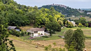 Paisagem rural com casas, árvores e uma colina ao fundo.