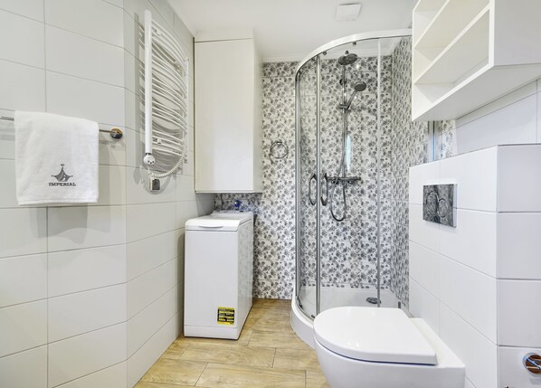 Uma casa de banho compacta com sanita, cabine de duche e máquina de lavar roupa integrada.