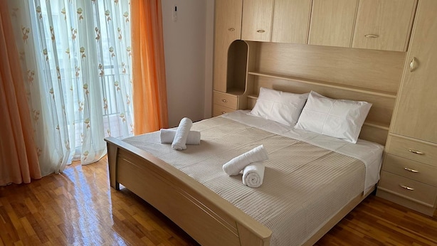 Cama bem arrumada com roupa de cama e toalhas brancas, cabeceira de madeira e guarda-roupa de madeira com gavetas.