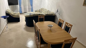 Uma área de refeições com mesa e cadeiras de madeira, um sofá azul e um banquinho estampado.