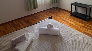 Quarto com cama, uma mesinha e janela com cortinas verdes.