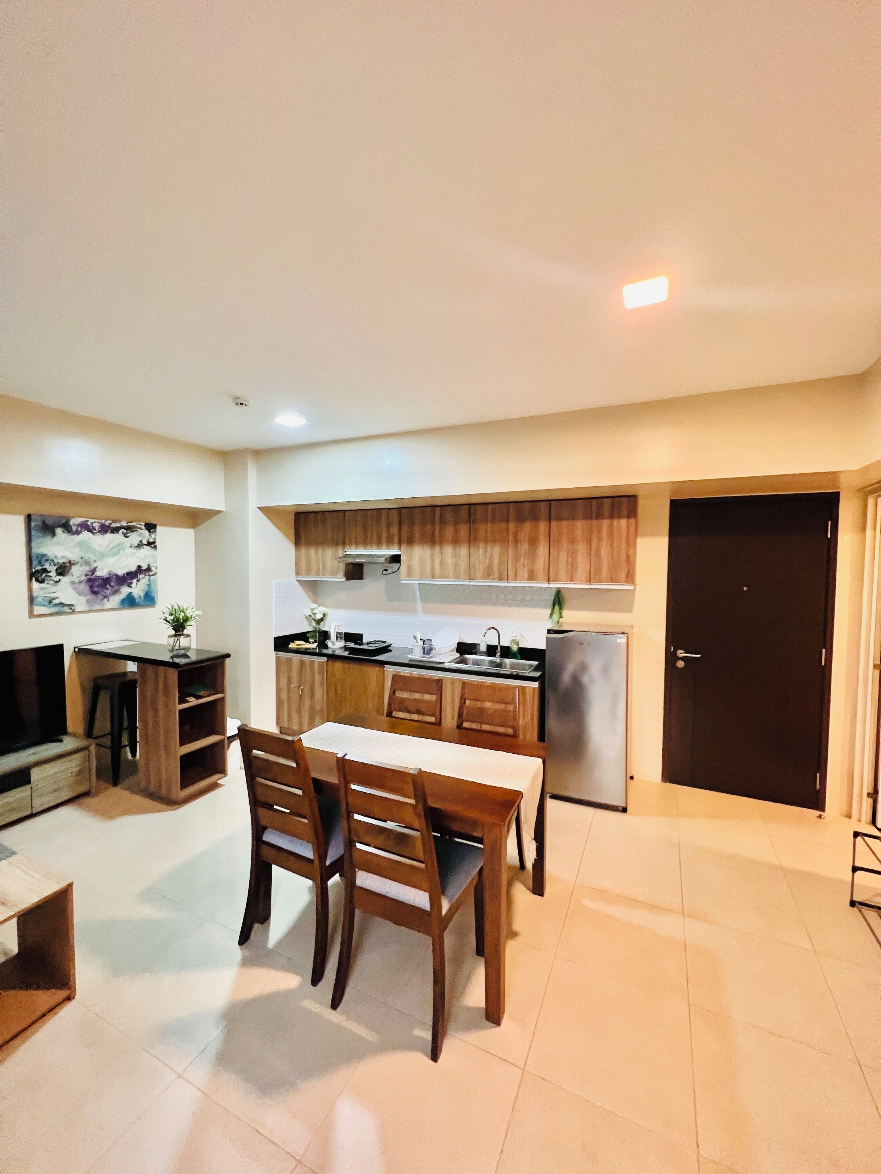 Uma cozinha compacta com armários de madeira, uma mesa de jantar com cadeiras, uma geladeira e uma TV em um móvel.