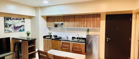 Uma cozinha compacta com armários de madeira, uma mesa de jantar com cadeiras, uma geladeira e uma TV em um móvel.