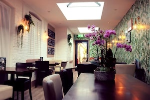 Restaurante com teto alto, iluminação pendente e um arranjo central de orquídeas.