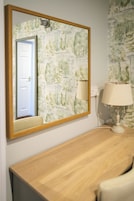 Quarto com escrivaninha de madeira, espelho na parede e uma luminária.