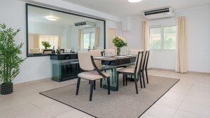 Uma área de jantar moderna com mesa de vidro, cadeiras, um espelho grande e um vaso com planta.