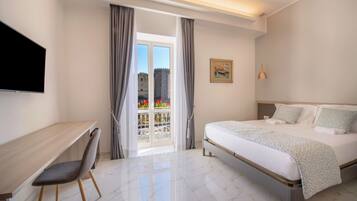 Quarto de hotel com cama, escrivaninha, cadeira, televisão e varanda com vista para um castelo.
