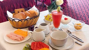 Mesa de café da manhã com pão, doces, frutas, bebida e uma sobremesa pequena.