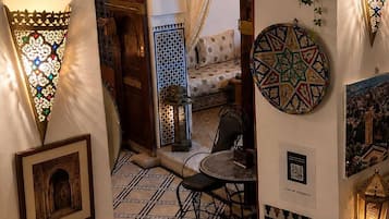Decoração em estilo marroquino com piso de azulejos, área de jantar com mesa e cadeiras, arte decorativa na parede e luminárias tradicionais.