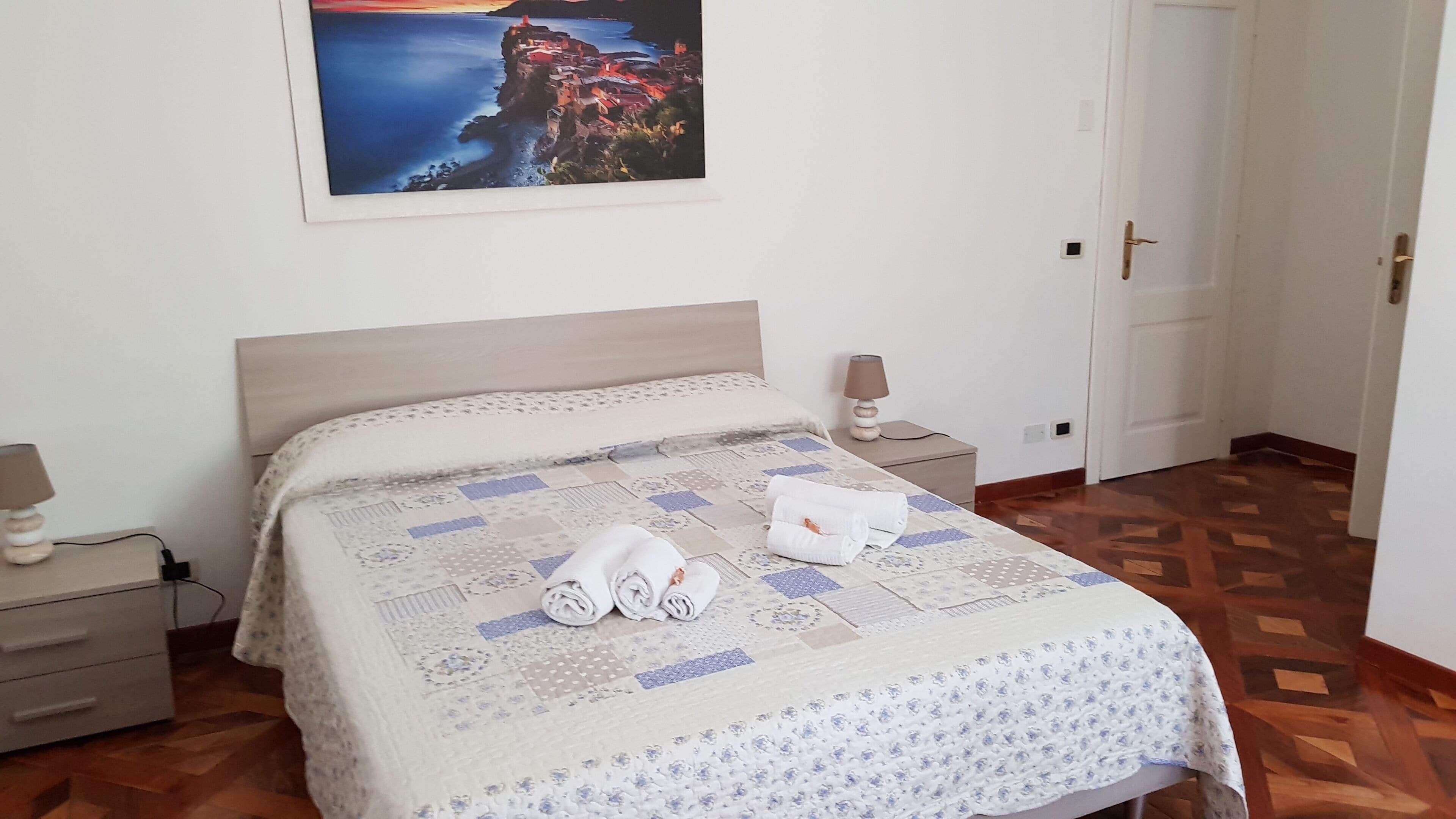 Cama bem arrumada com colcha, duas toalhas enroladas e abajur.