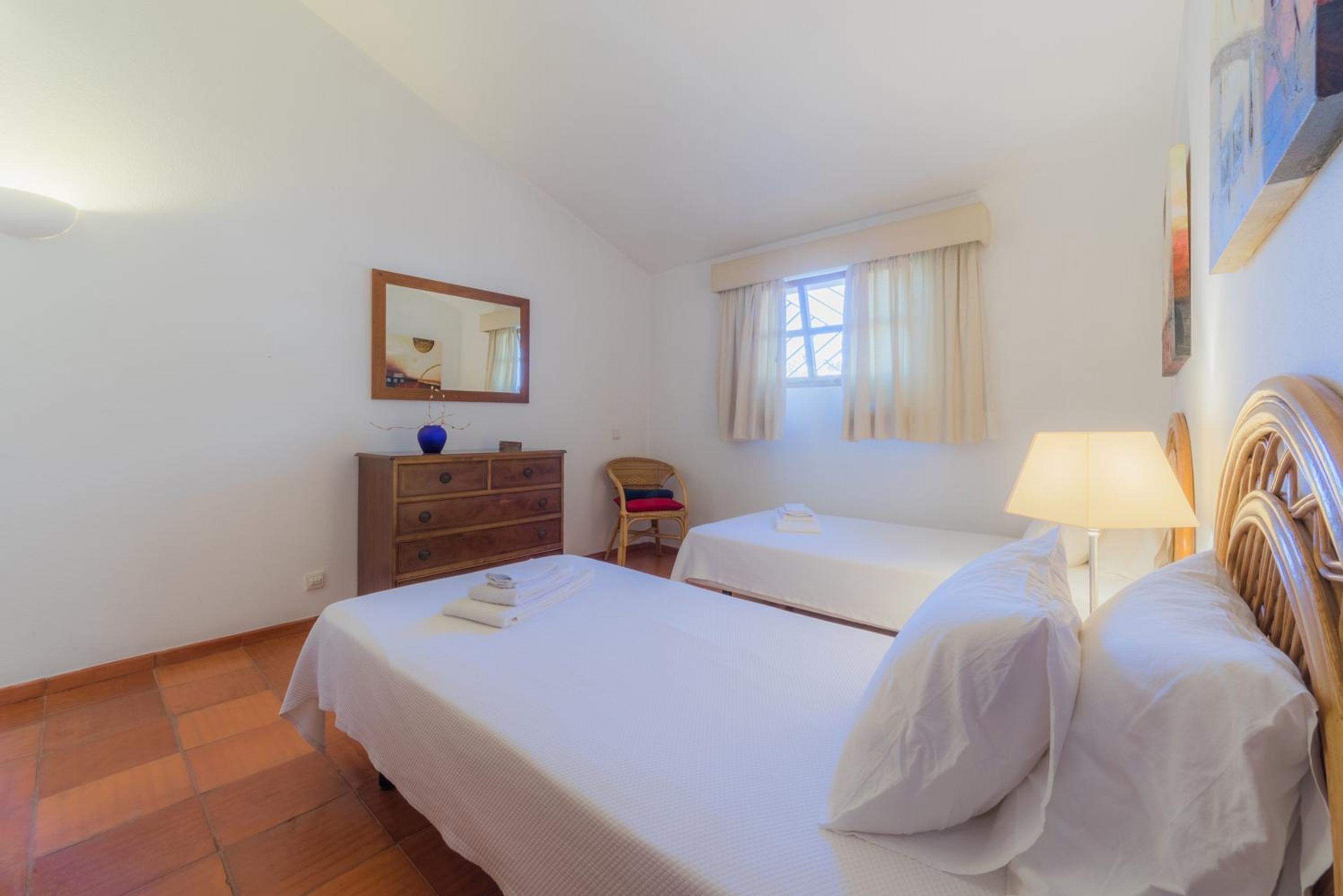 Quarto de hotel com duas camas, um penteado, uma cadeira, uma janela com cortinas e um abajur.