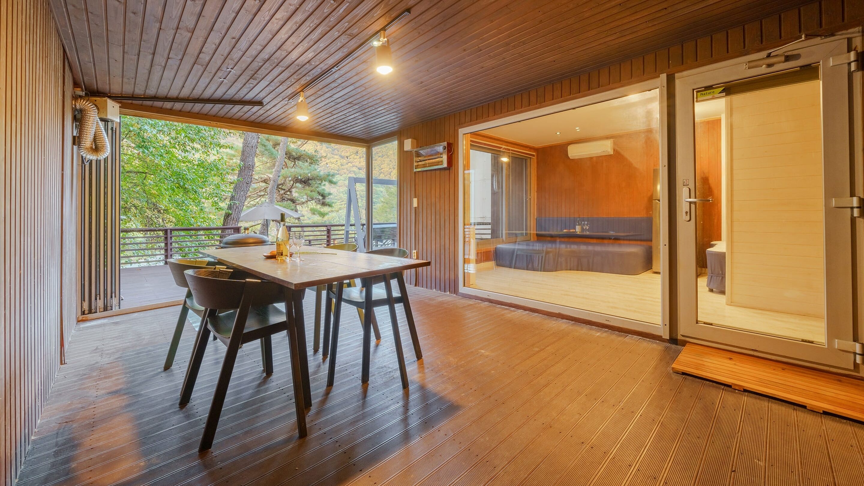 Interior moderno em madeira com área de jantar, porta de vidro deslizante para uma área de estar e um ar condicionado visível.