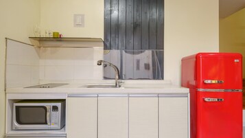 Uma cozinha compacta com bancada branca, pia de aço inoxidável, geladeira vermelha e micro-ondas.