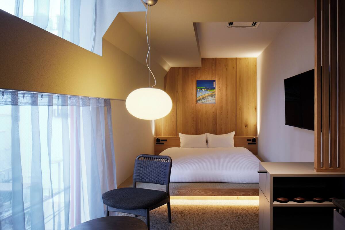 Quarto de hotel moderno com uma cama grande, uma escrivaninha, uma cadeira, uma televisão e um quadro na parede.
