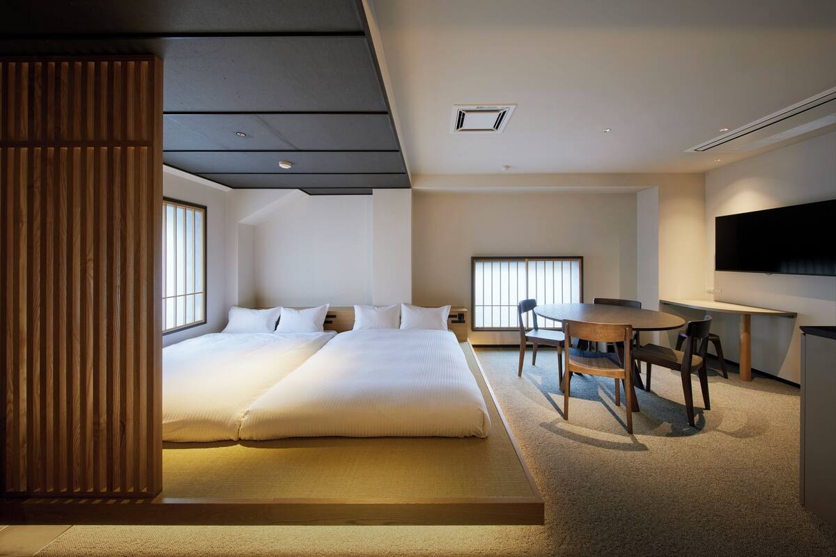 Quarto de hotel moderno com uma cama grande, área de refeições e televisão na parede.