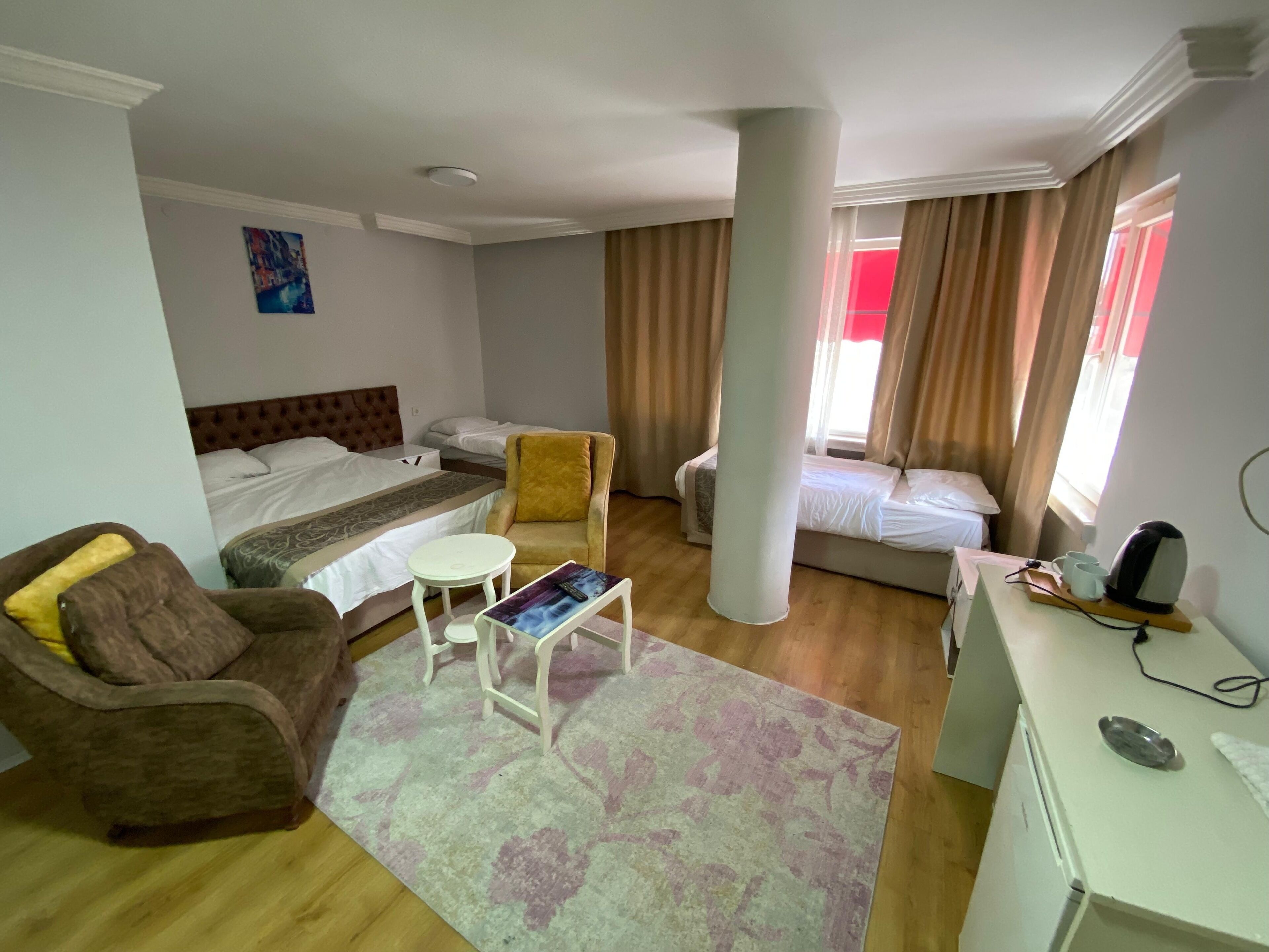 Quarto de hotel com uma cama, sofá, mesa pequena, escrivaninha e janela com cortinas.