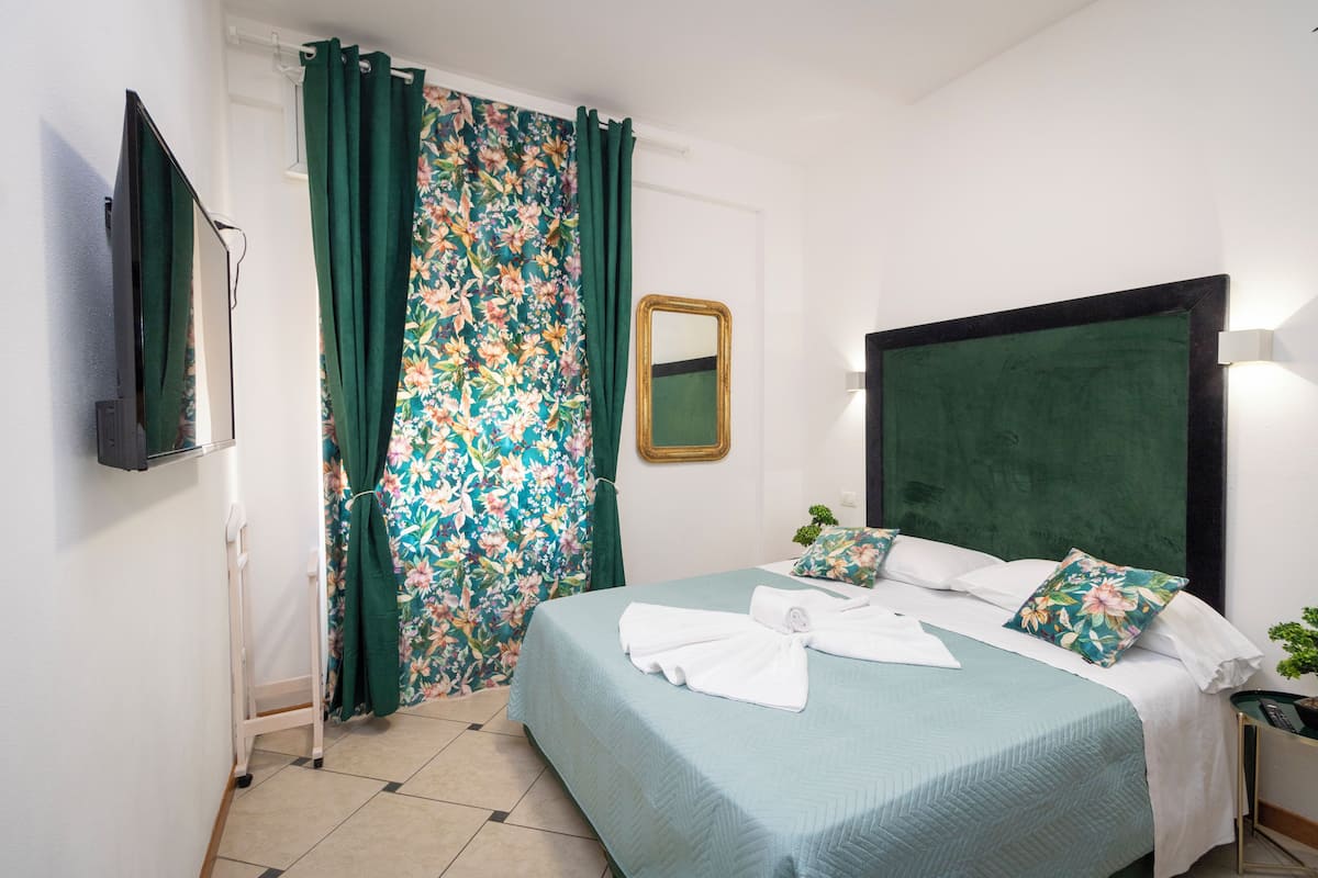 Quarto de hotel com cama, espelho, televisão e janela com cortinas.