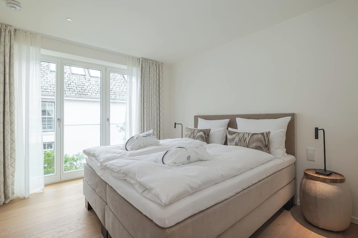 Quarto moderno com uma cama grande, uma mesa de cabeceira e vista através de uma porta deslizante.