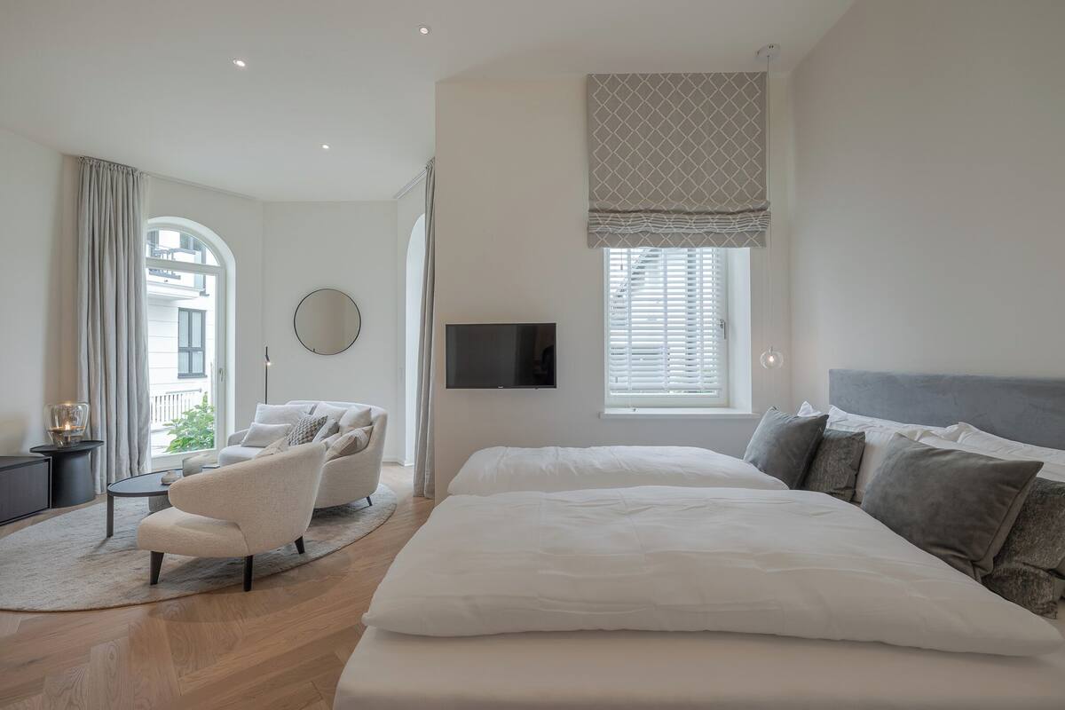 Quarto moderno com cama grande, sofá, televis ão e janela com persianas.