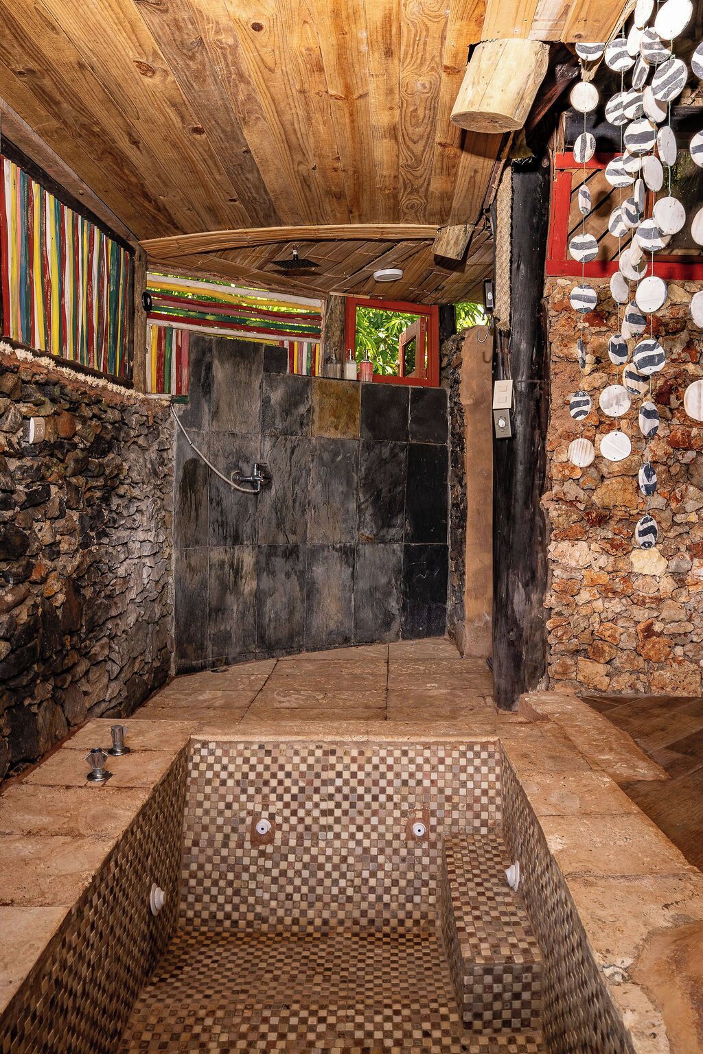 Um banheiro rústico com paredes de pedra, piso xadrez e vigas de madeira no teto.