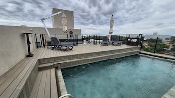 Piscina no terraço com deck de madeira, espreguiçadeiras e guarda-sóis.