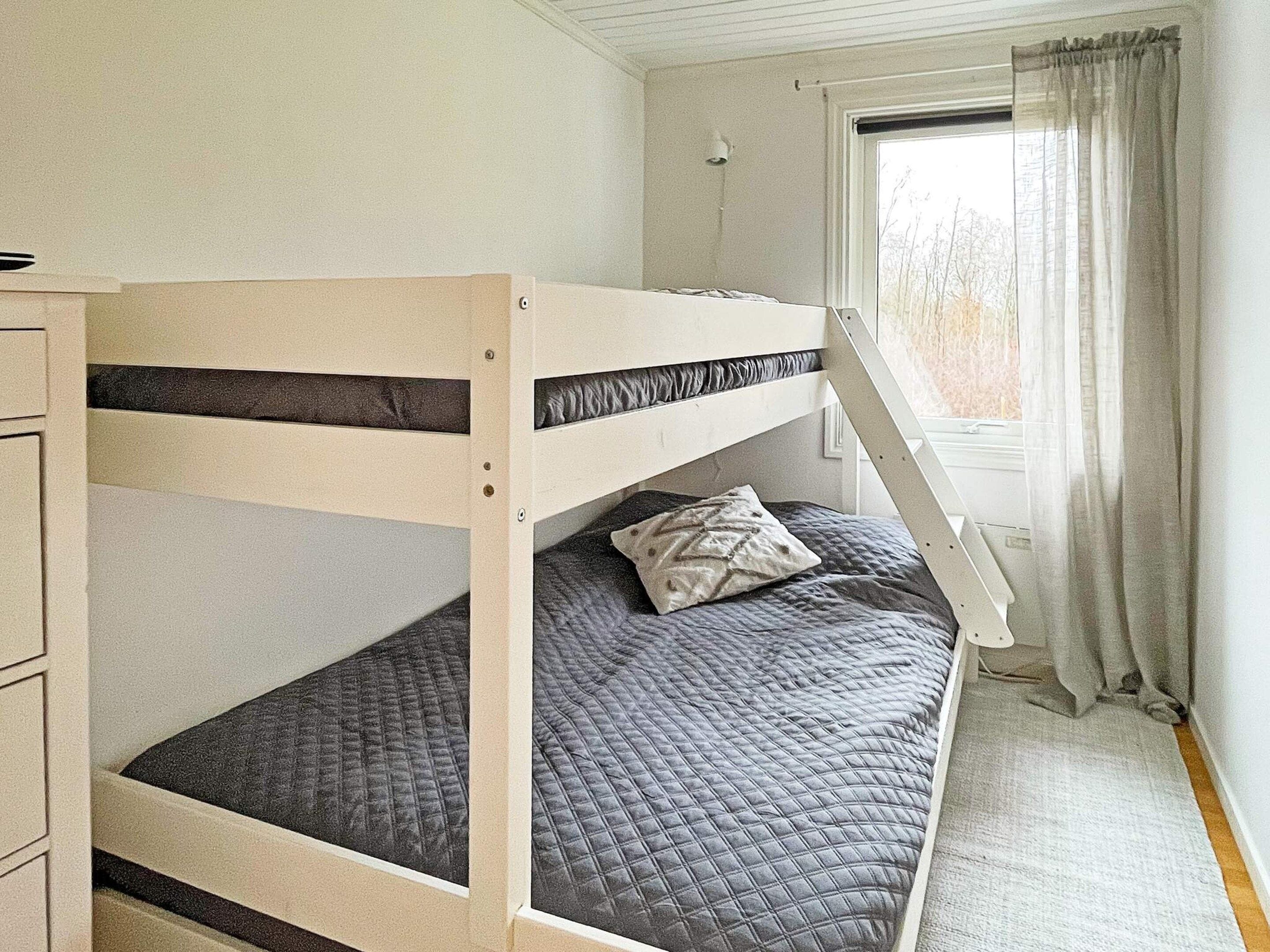 Uma cama beliche com escrivaninha e janela com cortinas.