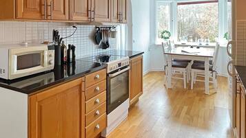 Cozinha com armários de madeira, micro-ondas, forno e área de jantar com mesa e cadeiras.