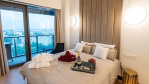 Quarto de hotel moderno com uma cama grande, uma varanda com vista para a cidade e uma luminária redonda na parede.