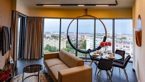 Uma sala de estar moderna com um sofá, uma mesa redonda e vista para a paisagem urbana através de grandes janelas.