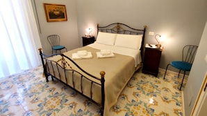 Uma cama bem arrumada com roupa de cama branca, duas mesas de cabeceira com abajures e uma cadeira com almofada azul.