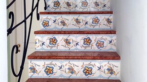 Escadaria com azulejos florais detalhados e guarda-corpo de metal preto.