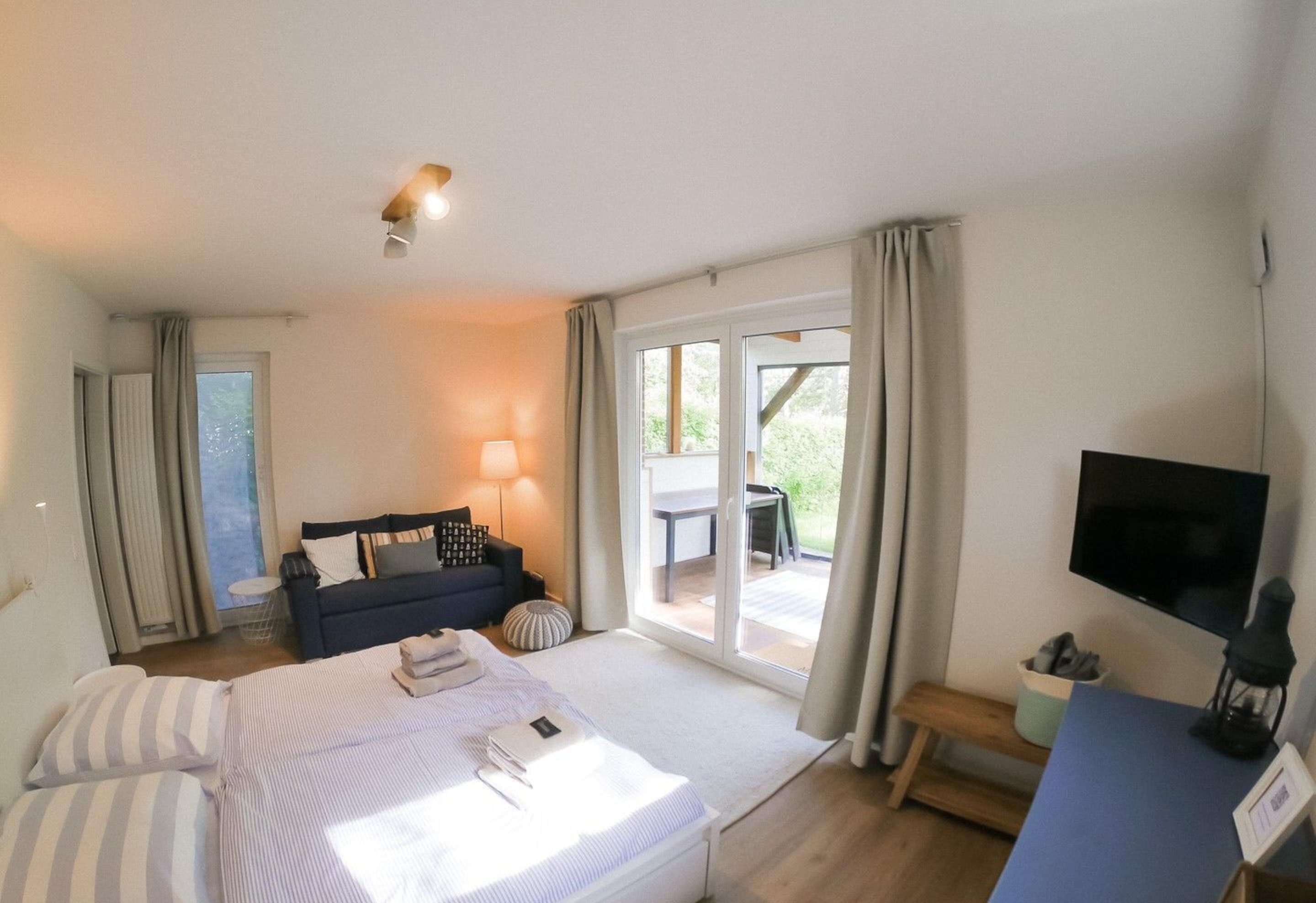 Quarto de hotel com cama, escrivaninha, televisão e varanda com mesa e cadeiras.