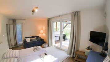 Quarto de hotel com cama, escrivaninha, televisão e varanda com mesa e cadeiras.