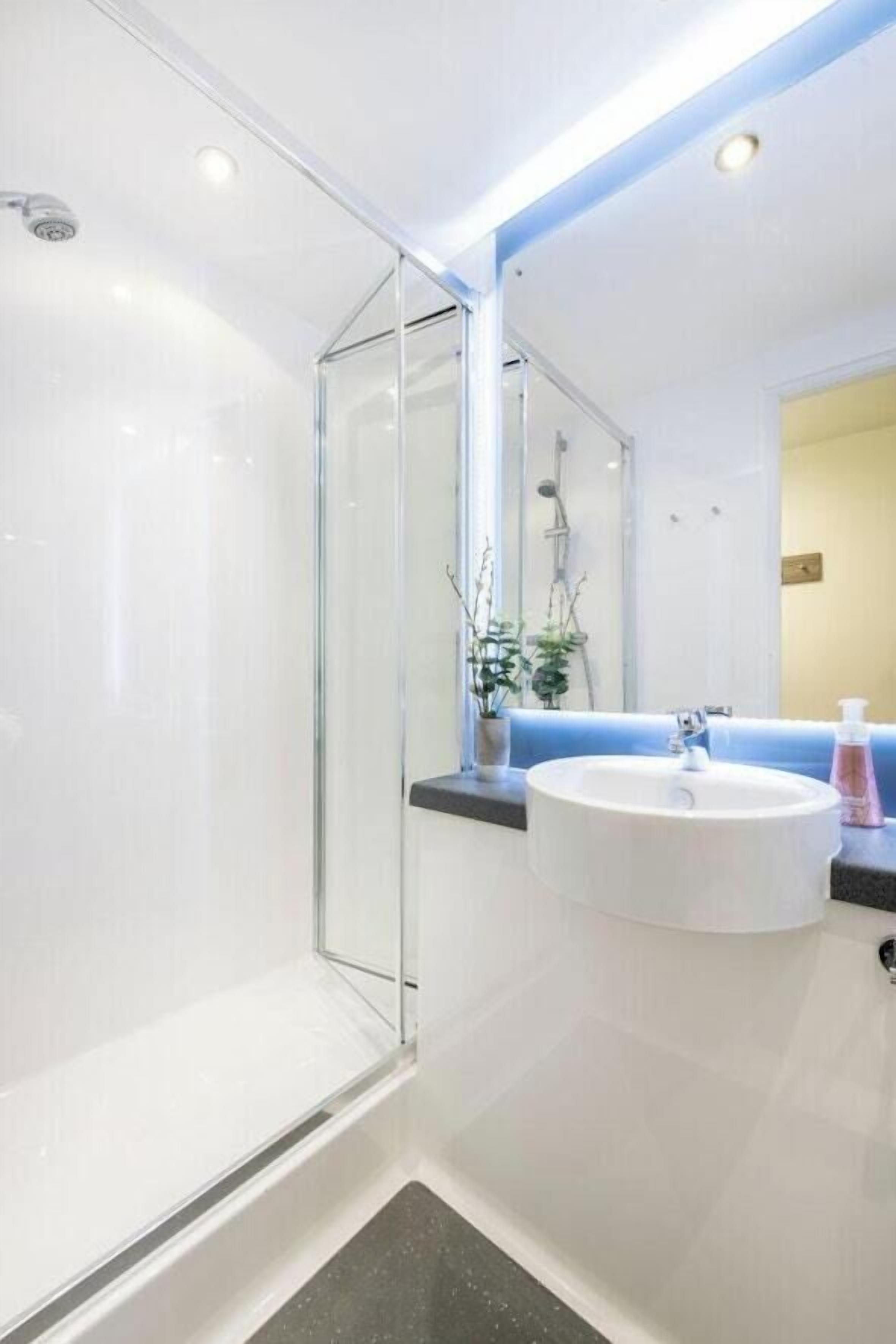 Casa de banho moderna com cabine de chuveiro em vidro, lavatório branco e espelho.
