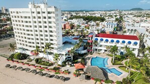 Hotel com vários andares, piscina e área de praia com guarda-sóis e espreguiçadeiras.