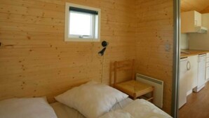 Quarto de cabana de madeira com cama, uma mesinha, janela e cozinha compacta.