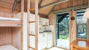 Interior de uma cabana de madeira com beliche, cozinha compacta e área de jantar com vista para o exterior.