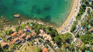 Vista aérea de uma área costeira com águas turquesa cristalinas, uma praia de areia e uma área residencial com casas e uma quadra de tênis.