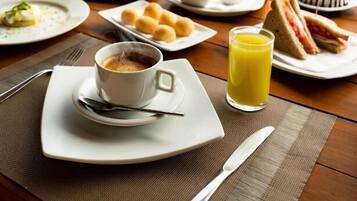 Mesa de café da manhã à beira da piscina, com pratos de comida, uma xícara de café e um copo de suco de laranja.