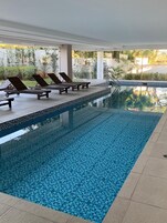 Piscina interior com chão em mosaico e espreguiçadeiras.