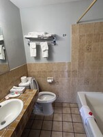Casa de banho com lavatório, sanita e banheira. Há um porta-toalhas com toalhas e um rolo de papel higiénico.