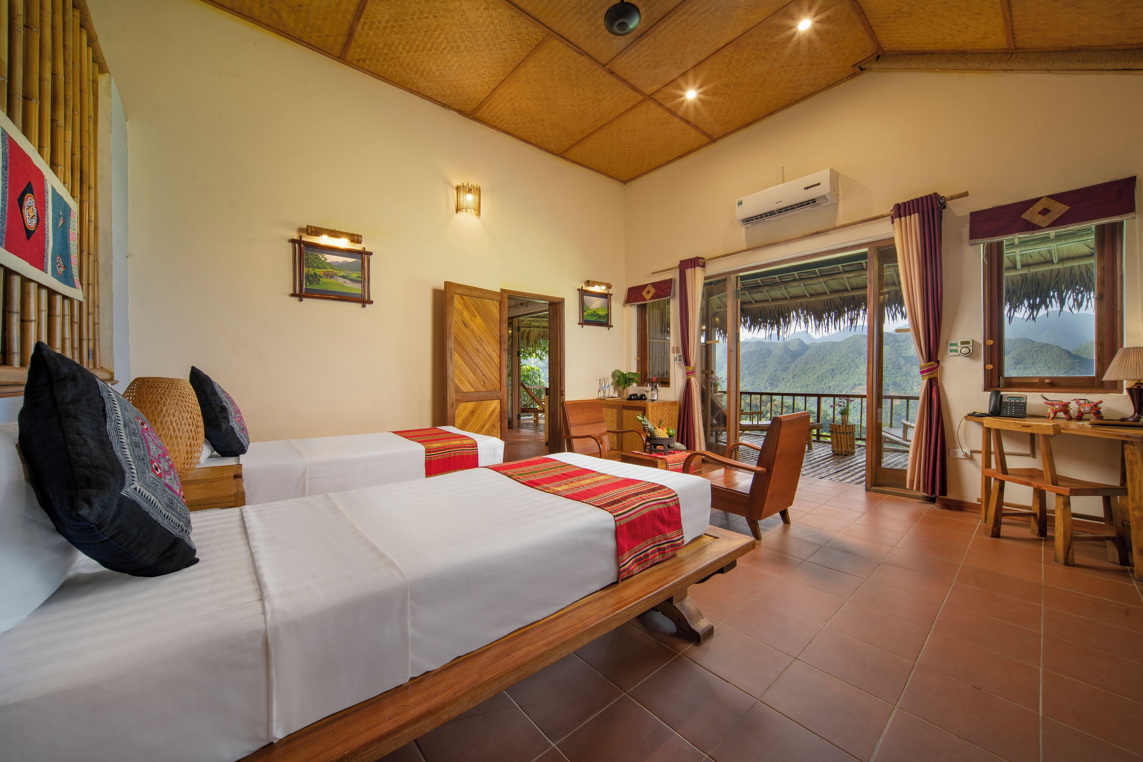 Quarto com duas camas, uma escrivaninha de madeira e vista para as montanhas.