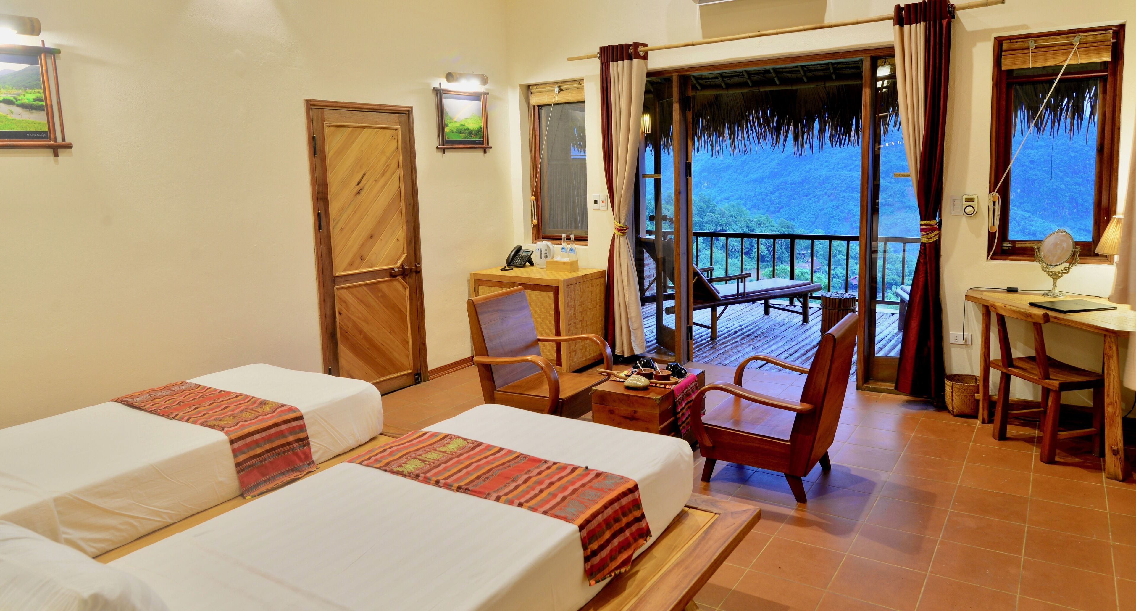 Quarto de hotel com duas camas, uma escrivaninha, uma cadeira e varanda com vista para as montanhas.